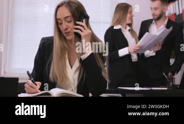 Happy young woman taking notes while talking on mobile phone. woman ...