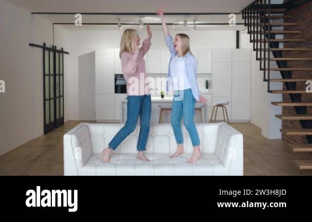 Happy family senior mom having fun with adult daughter dancing on sofa ...