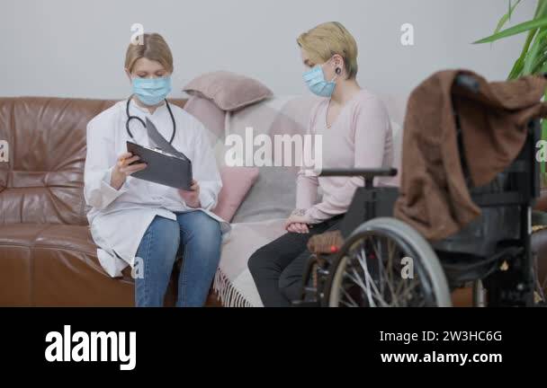 Serious focused doctor consulting disabled woman at home on coronavirus ...