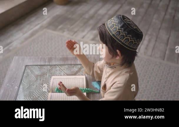 Adorable muslim kid read the Quran in prayer hat and arabic clothes ...
