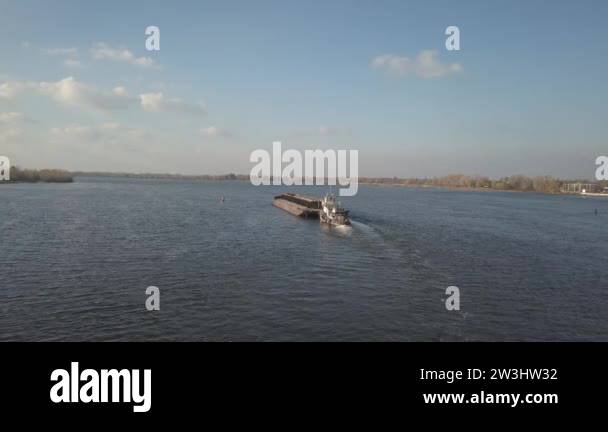 A tugboat ship pushes a barge upstream of the river to transport bulk ...