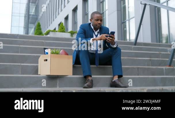 African American businessman sitting on stairs outdoors with box of ...