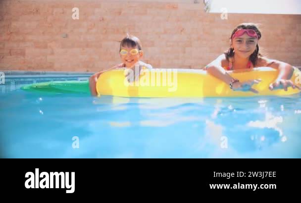 Young children splashing and floating on inflatable in swimming pool ...