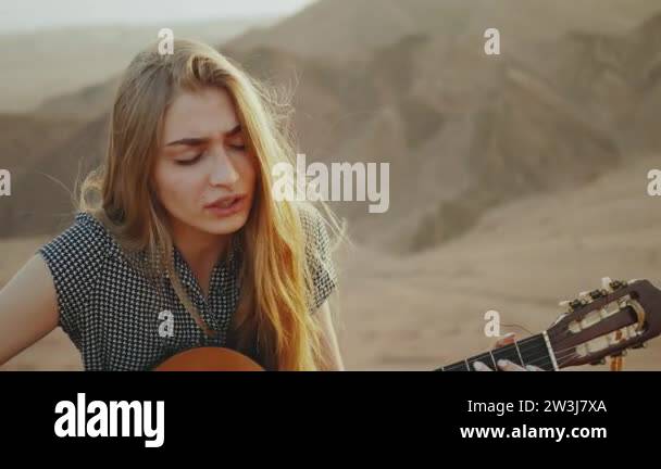 Woman playing guitar and singing in desert in sunset landscapes, desert ...