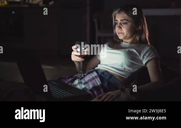 Upset woman drinking alcohol, watching a sad movie on TV at home ...