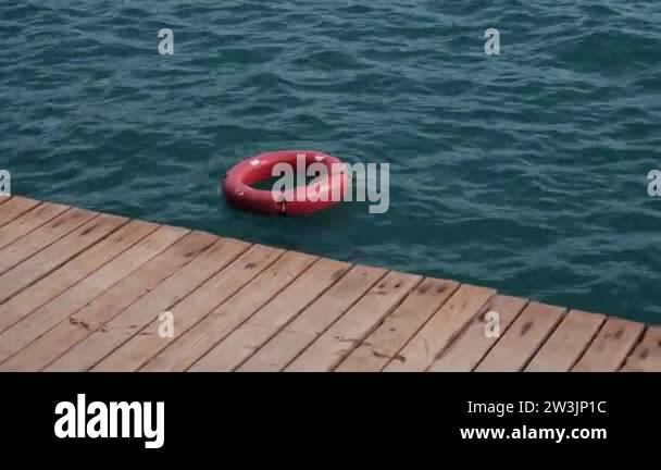 Red lifebuoy or safety ring floating near the dock in blue sea water ...