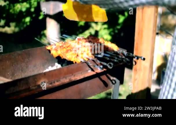 man fanning the heat in the grill under the meat,ashes from the coals ...