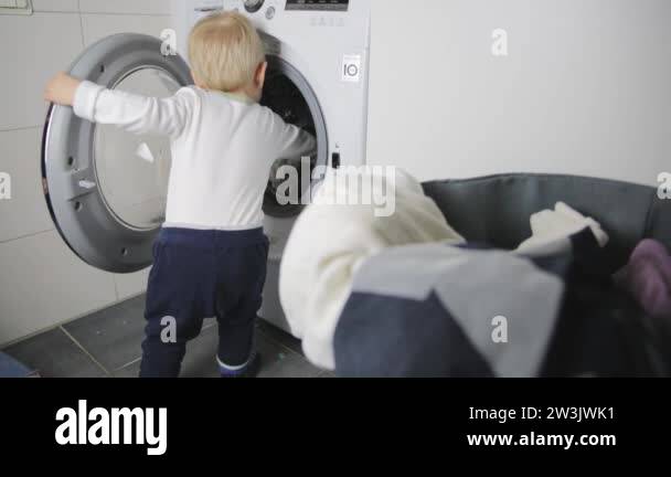 Two year old child doing household chores. Loading washing machine ...
