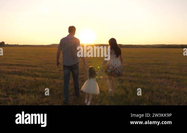 little daughter plays and jumps into field holding hands of mom and dad ...