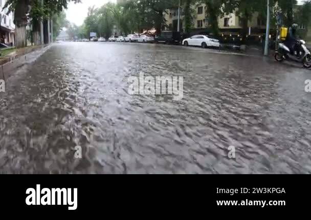 Heavy rain in the city. Streams of water along of the road. Cars drive ...