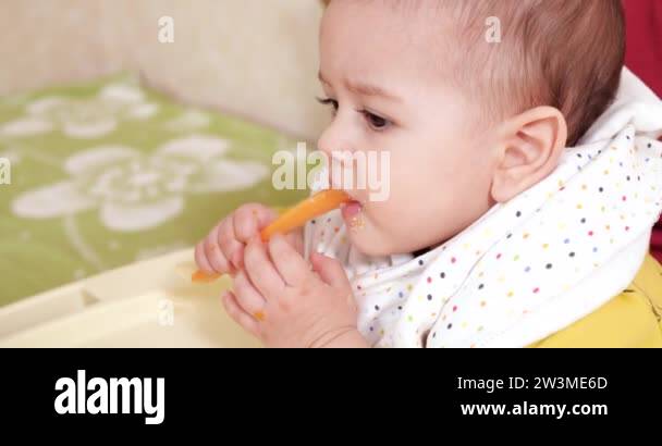 mother holds the baby in her arms and feeds her boy with a spoon ...