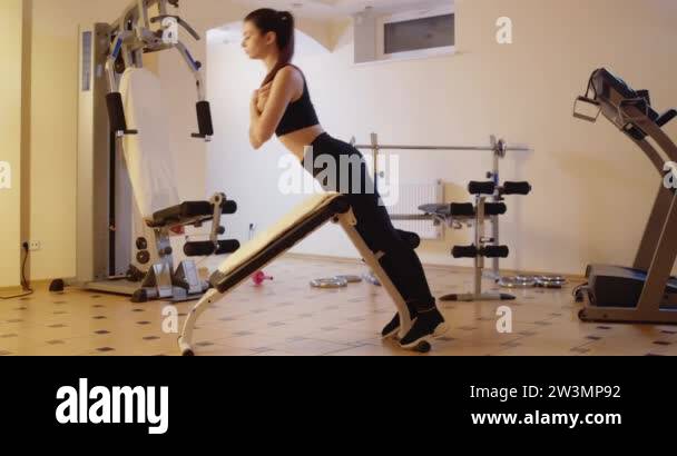 Wide shot side view of slender young woman training on exercise bench ...