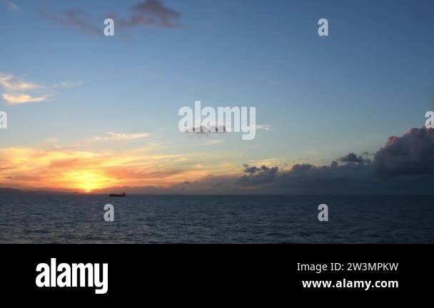 A sunset just as the sun goes below the horizon, with a cargo ship ...