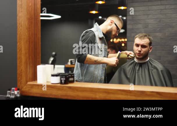 Barber in glasses cuts bearded mans hair with a clipper in barbershop ...
