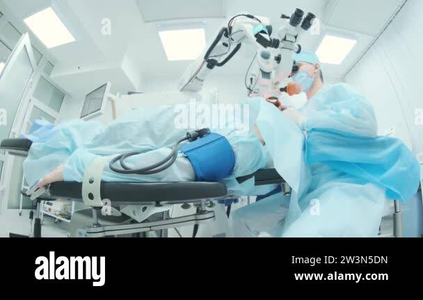 Surgeon looking into the microscope at the eye of female patient at the ...
