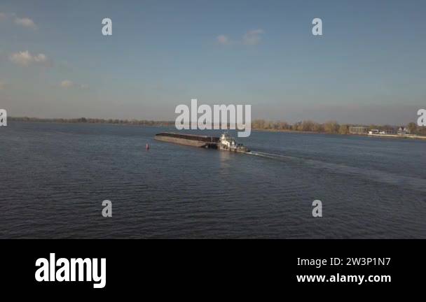 A tugboat ship pushes a barge upstream of the river to transport bulk ...