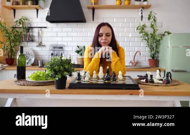 Young woman playing chess on kitchen table. Female plays in logical ...