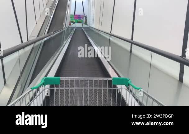 Shopping cart is pushed down the automatic sliding ramp inside the mall ...