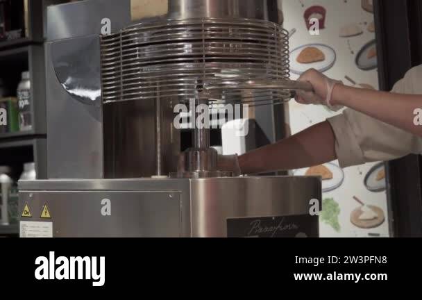 The hands of a chef in a fast food restaurant uses a pizza press tool ...