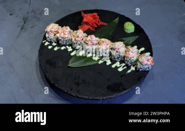 Appetizing sushi maki rotates on the black plate above grey background ...