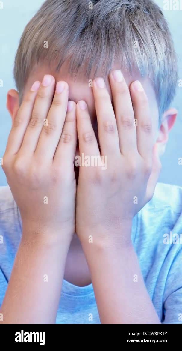 Boy covering his face with his hands and peering out with one eye ...