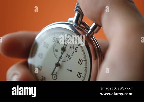 Male hand holding analogue stopwatch on orange color background. Time ...