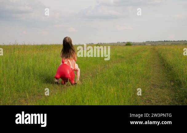 Happy little girl is playing in park and jumping on an inflatable toy ...