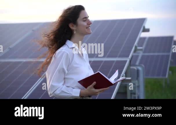 Woman looks at solar panels row on the ground at sunset and smile and ...