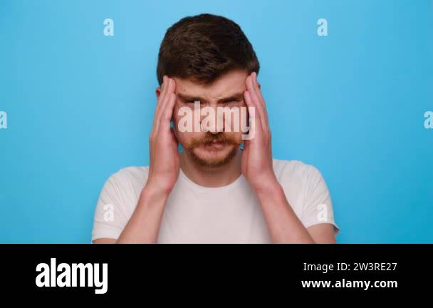Portrait of stressed unhappy young man calming down relieving headache ...