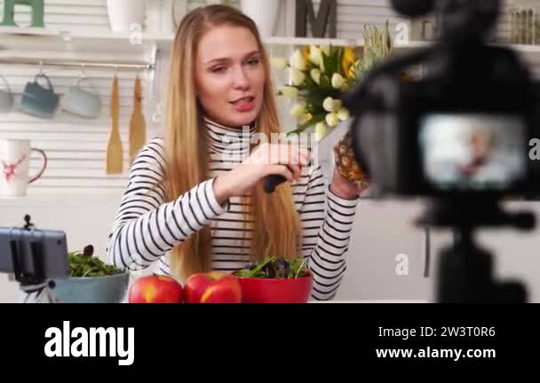 Food blogger cooking fresh vegan salad of fruits in kitchen studio ...