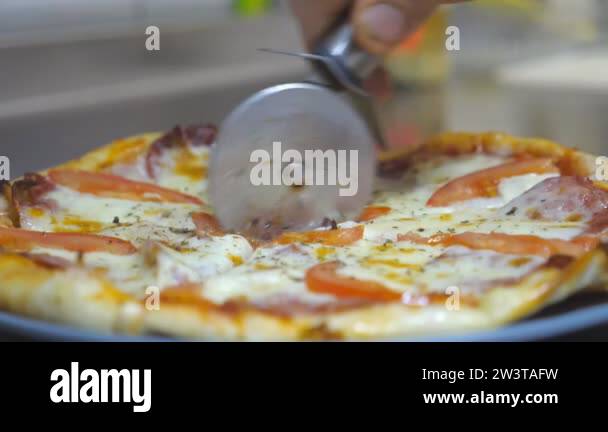 Close up male hand of chef cutting tasty pizza into slices with a round ...