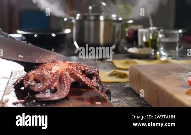Chef cutting boiled octopus with knife. Boiling saucepan and utensil in ...