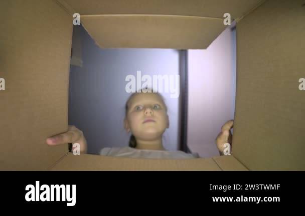A little girl opens a cardboard box and shouts happily. Inside view of ...