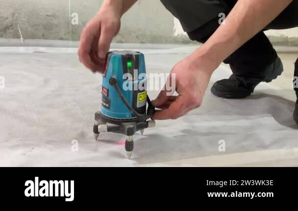Worker turning on laser level device cement floor measuring markers ...