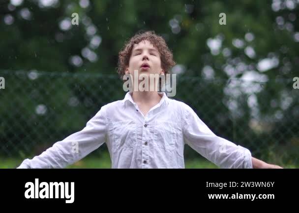 Portrait of cute young boy having fun catching rain drops. A curly ...