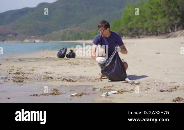 Man in gloves collects plastic trash on a beach. The problem of garbage ...