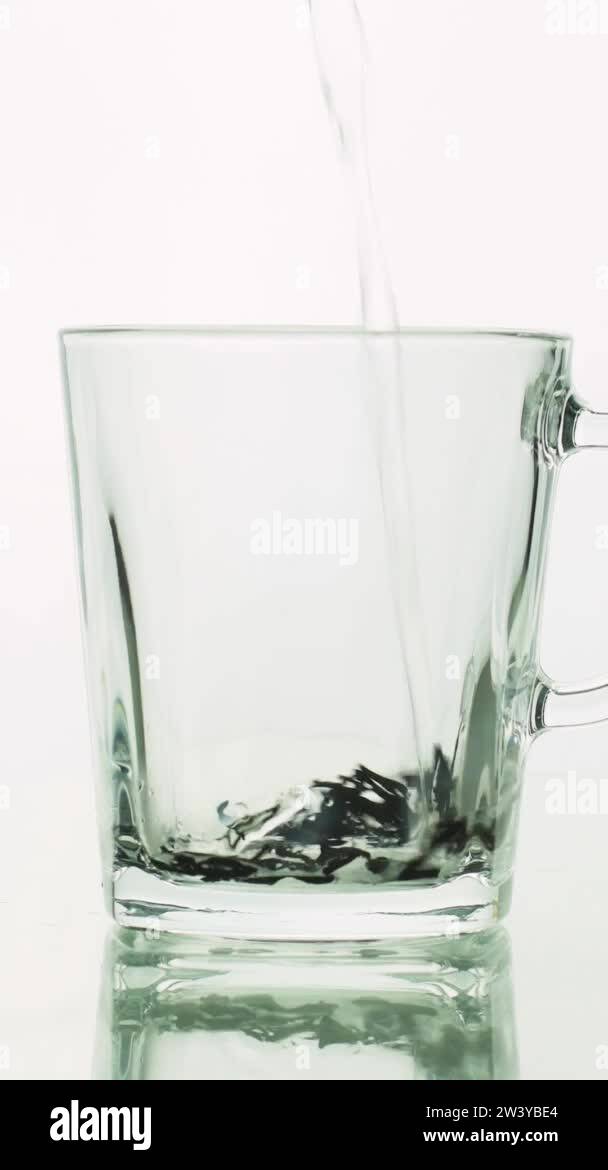 Vertical video black tea particles pouring into glass transparent mug ...