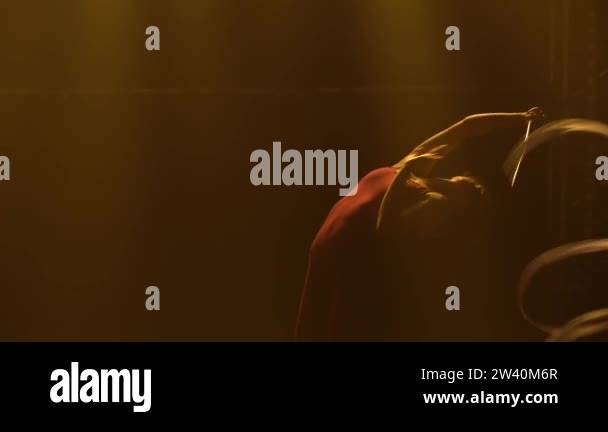 An active young girl performs gymnastics elements with a silk ribbon and does somersaults back ...