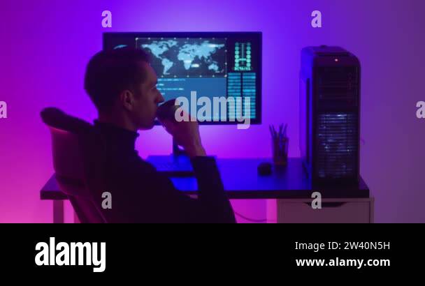 A male programmer drinks coffee while working at a computer in a data ...