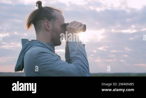 Side portrait of explorer looking into binoculars on nature sunny sky ...