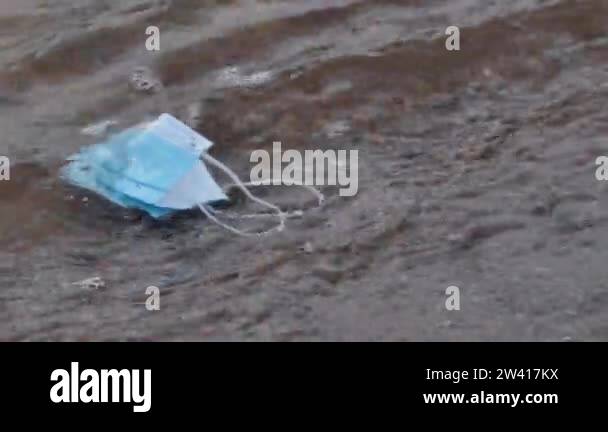 Medical disposable blue protective mask on the seashore, waste of the ...