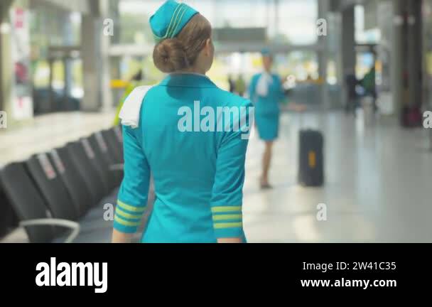 Back view of slim stewardess in blue uniform walking to colleague in ...