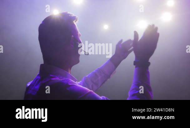 Portraot of man singer singing a song and clapping hands in spotlights ...