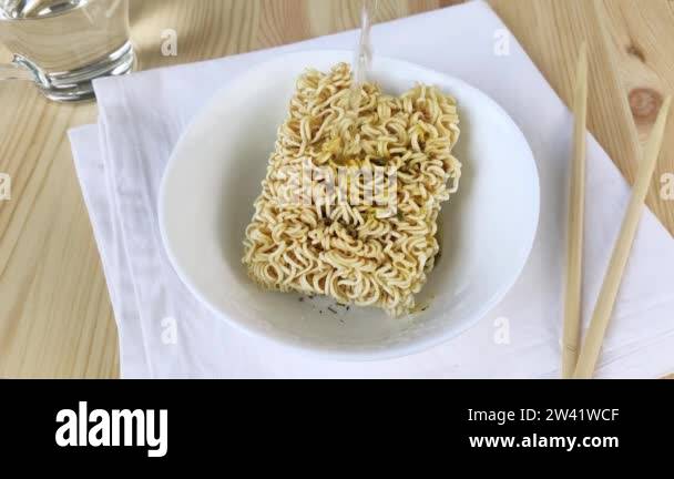 Egg noodles in plate are poured with boiling water. Instant ramen soup ...
