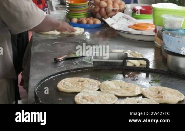 Handheld footage of men spreading "roti canai" and cook before serve to ...
