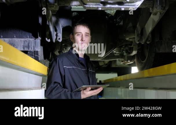 Positive young mechanical engineer stands under truck with tablet to ...