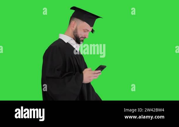 Graduate student walking and texting message on the phone on a Green ...