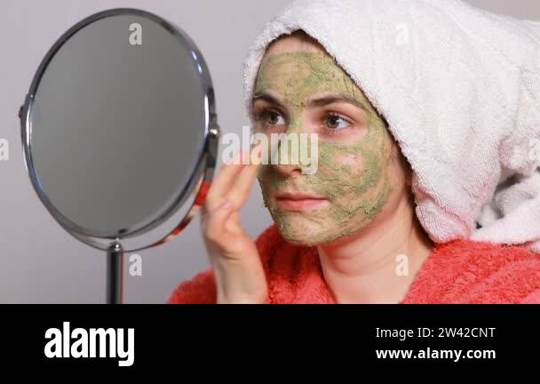 A young woman in a pink bathrobe applies an Ayurvedic blend of ubtan to ...
