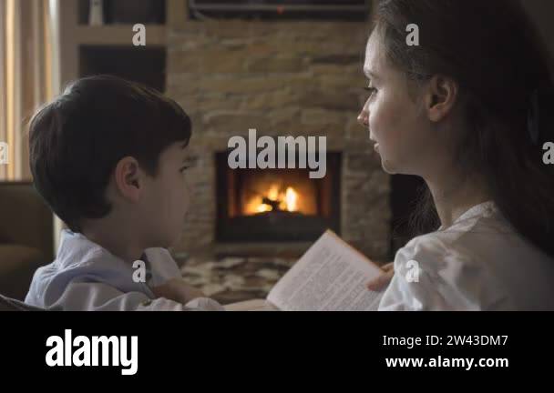 Mother and son at the fireplace where the fire is burning learn poems ...