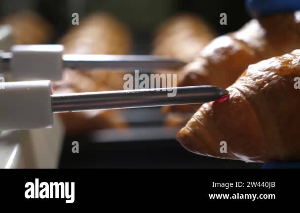 Well cooked croissants getting jam stuffing from two metallic sticks in ...